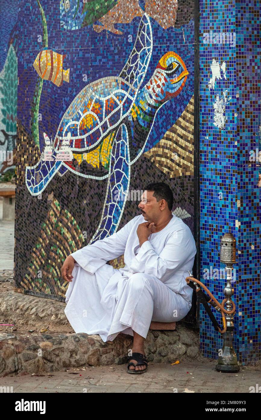 MAN IN A TRADITIONAL WHILE DJELLABA WITH HIS HOOKAH, ENTRANCE TO THE ...