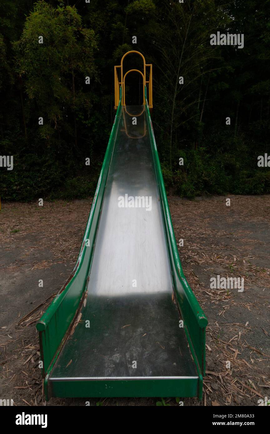 A metal slide starts against the green of a forested area and ends at ...