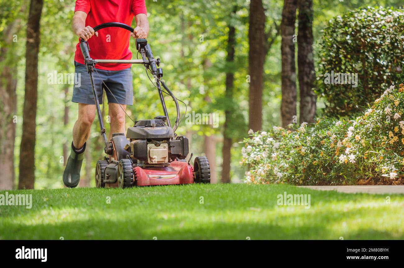 Mowing grass with a gas powered lawn mower. Male landscaper cutting ...