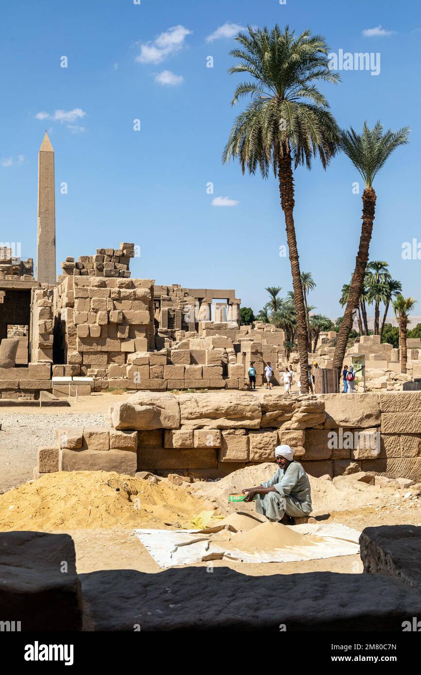 MAN SIFTING SAND IN THE BRIGHT SUN, RUINS AND OBELISK, PRECINCT OF AMUN ...