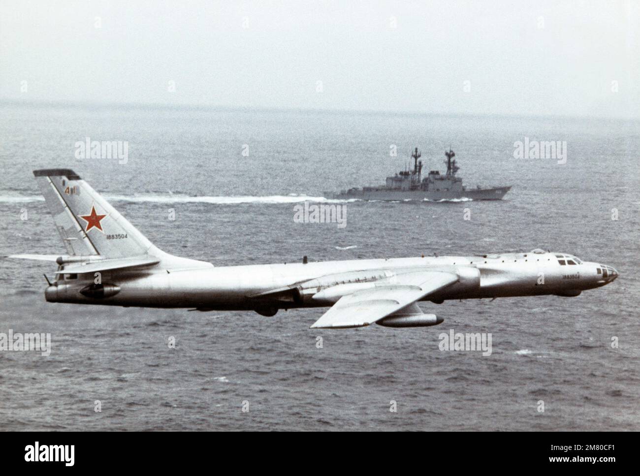 A Soviet Tu-16 Badger aircraft flies near a U.S. Navy destroyer ...