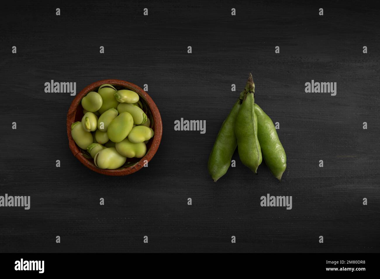 freshly peeled green beans in a clay bowl with a bunch of broad beans ...