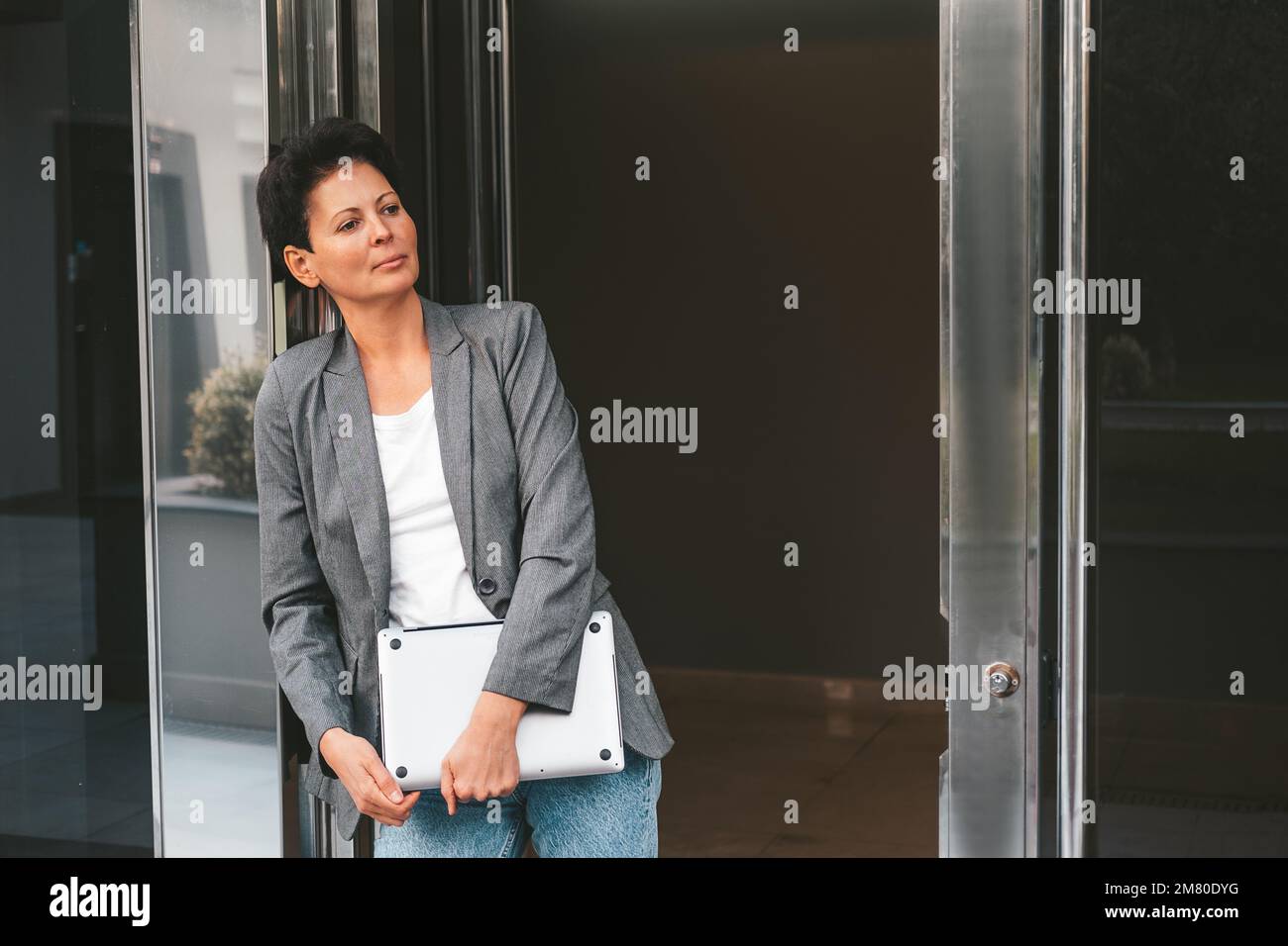Business woman in jacket and with laptop near door to business center ...