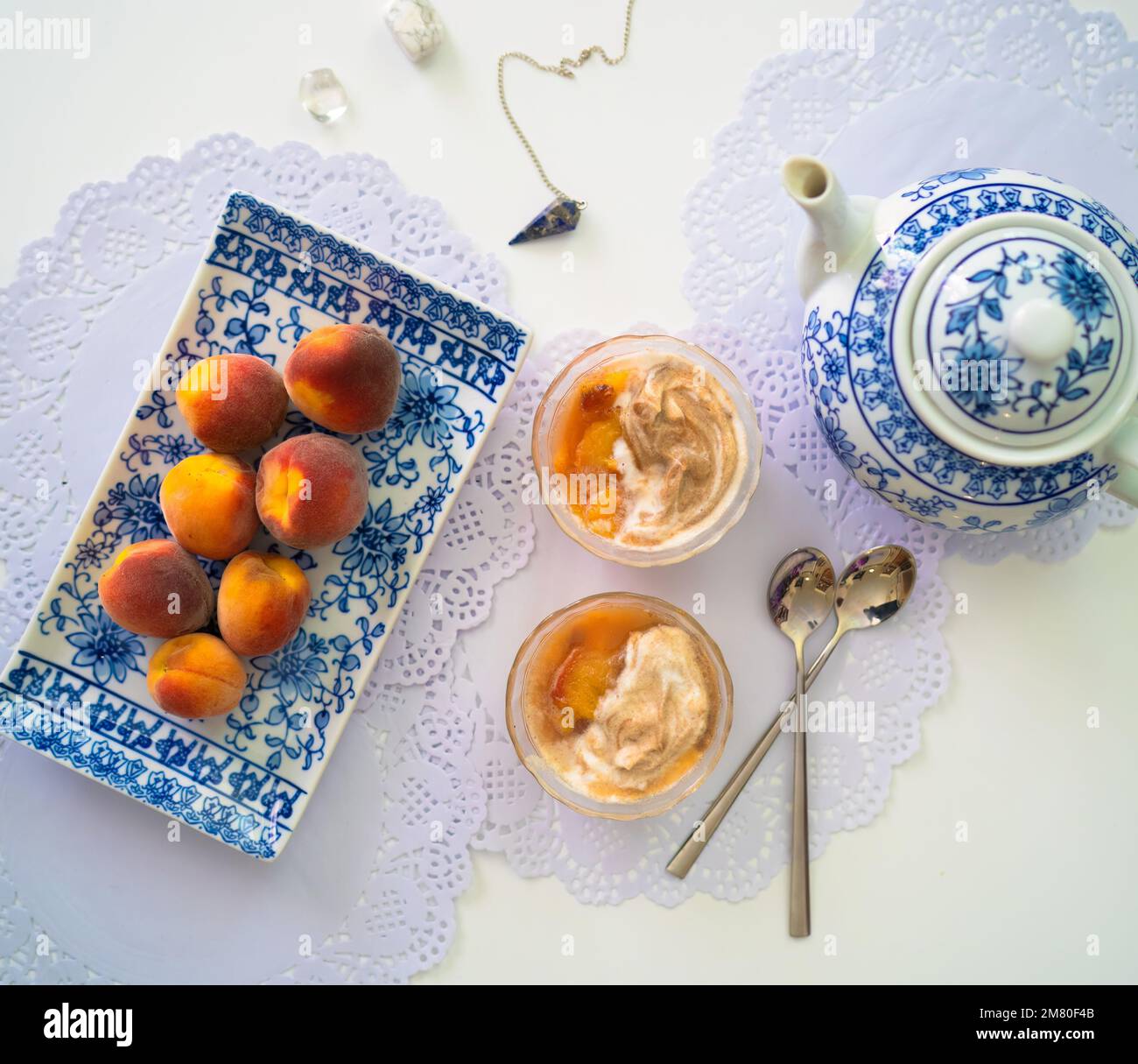 A closeup of fresh peaches with cream and a teapot with a blue floral ...