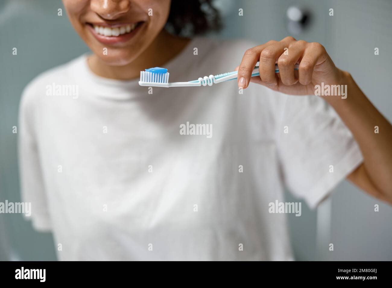 Close up of woman brushing teeth in bathroom and looking at camera ...