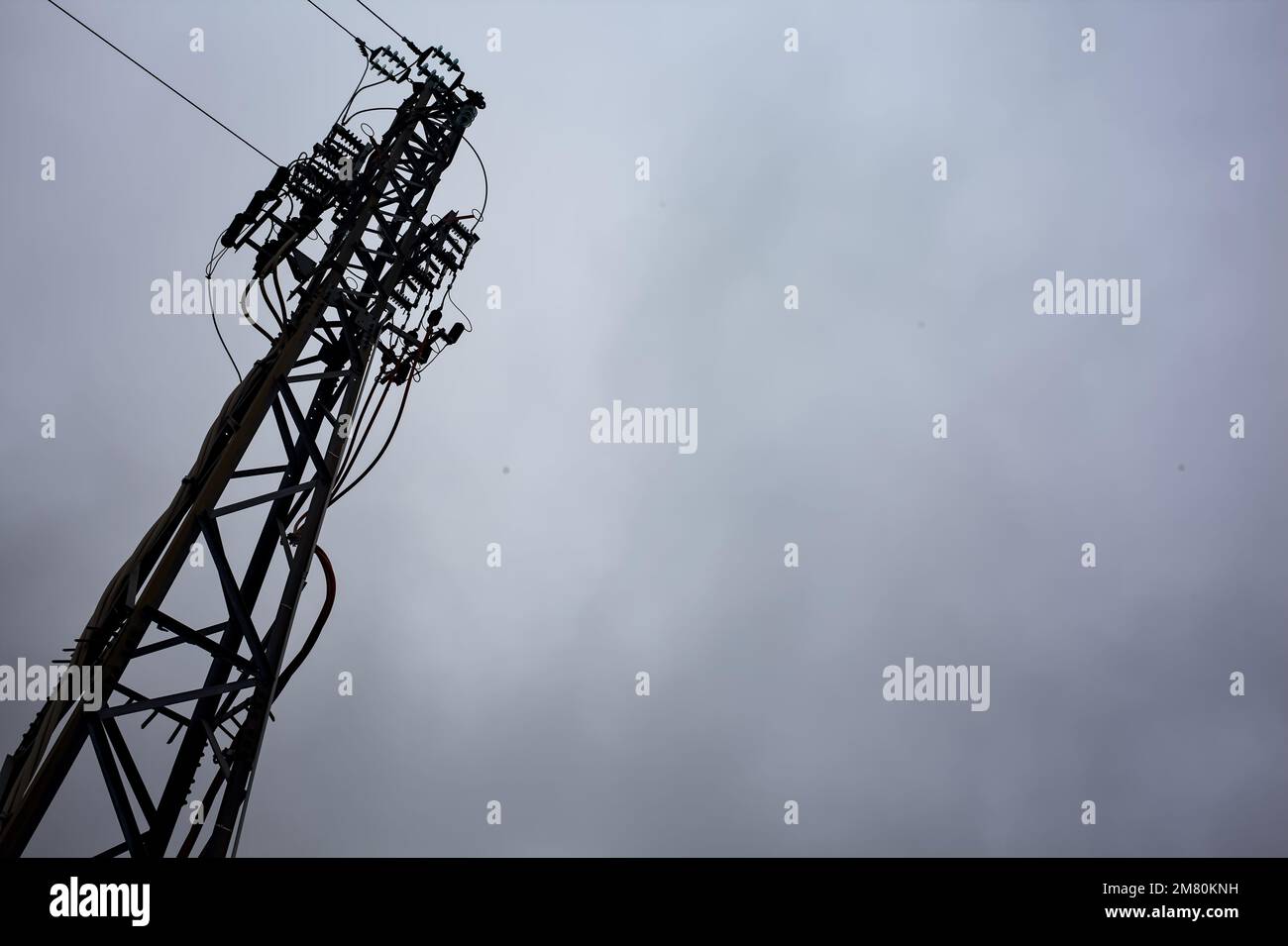 Electricity pylon with over head cables passing on it and a cloudy sky ...