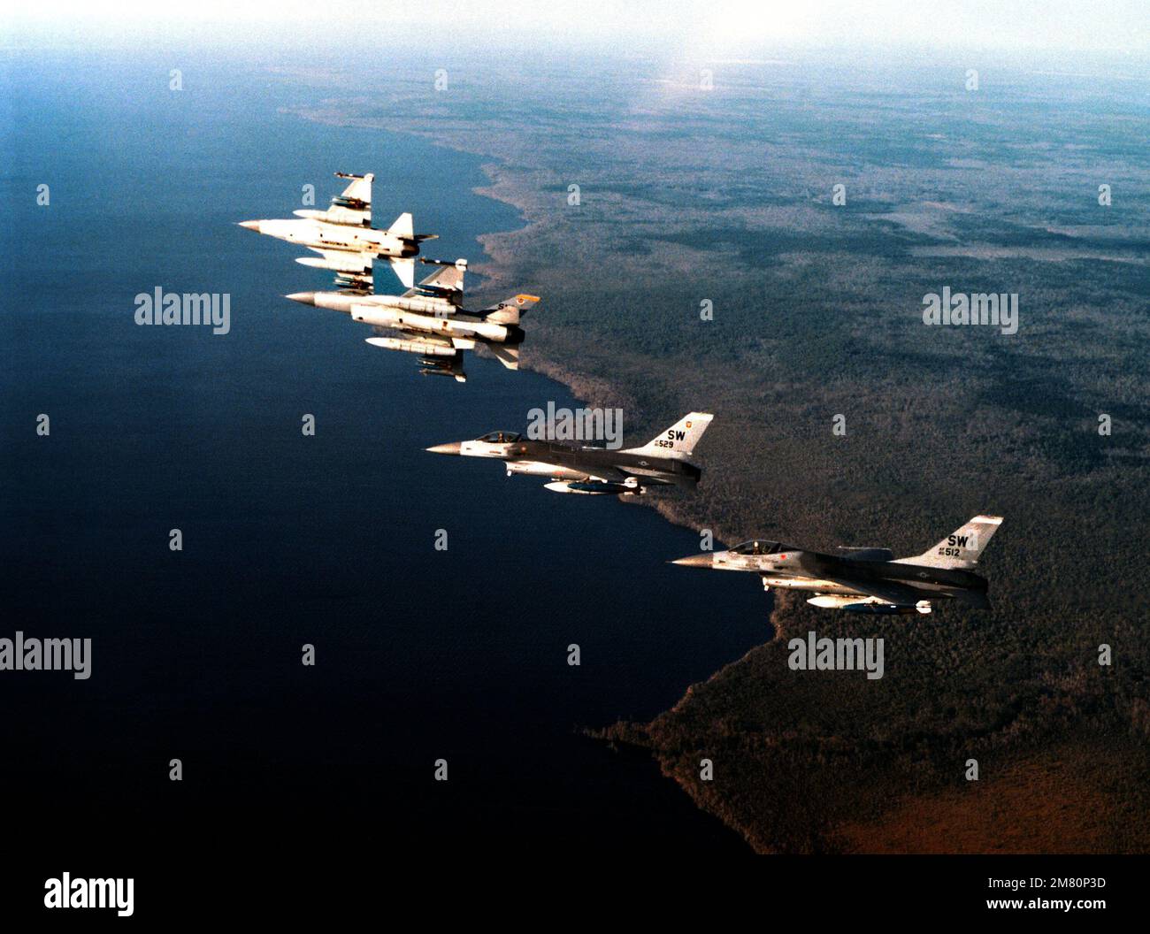 An air-to-air left side view of four F-16A Fighting Falcon aircraft in ...