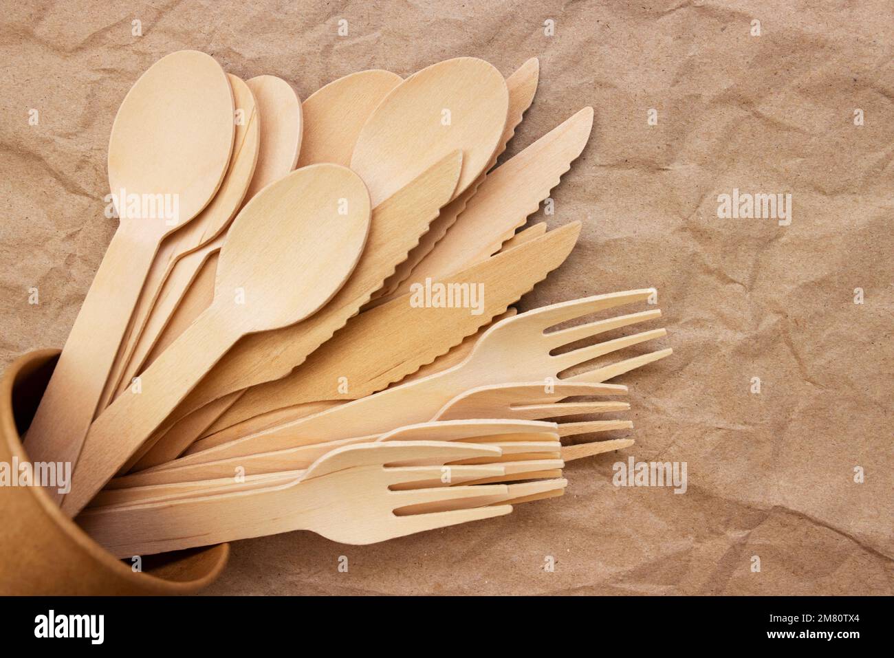 Wooden forks, spoons and knifes in cardboard cup on crumpled paper ...