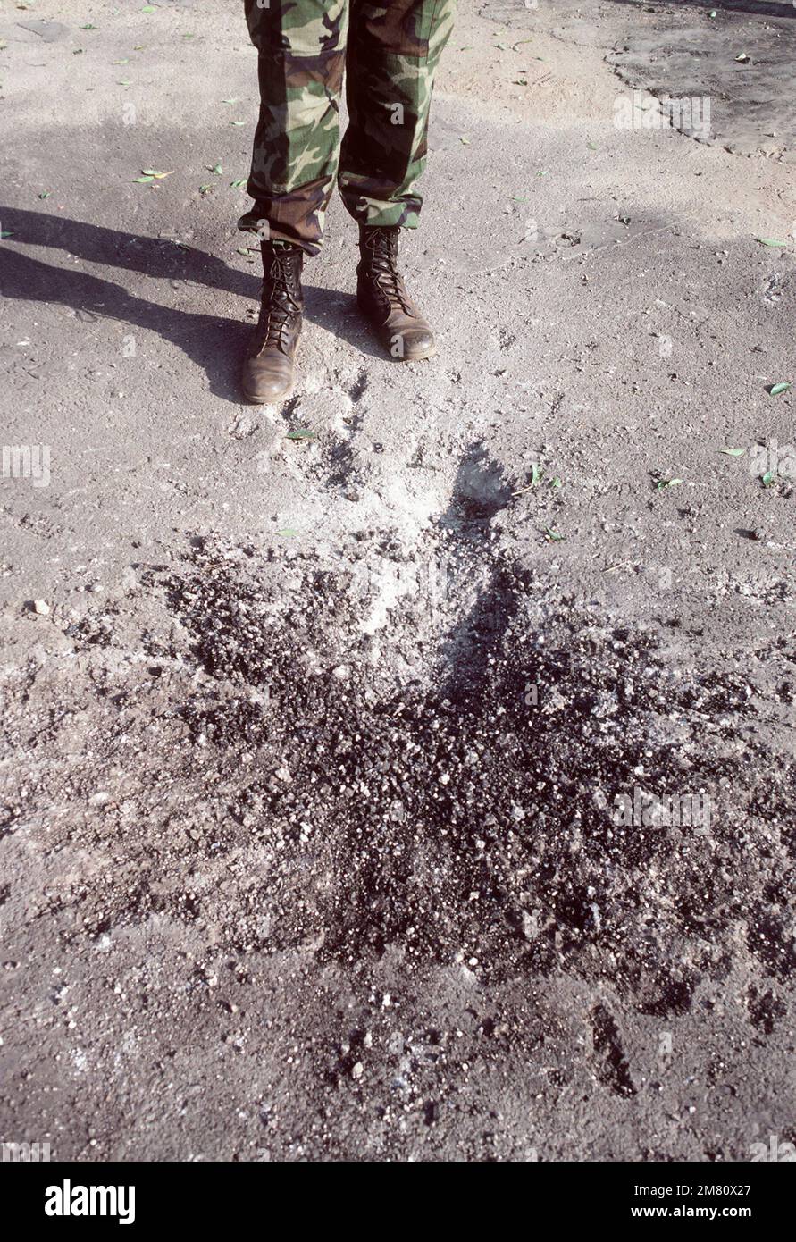 A Marine examines the impression made by a mortar round in a concrete ...