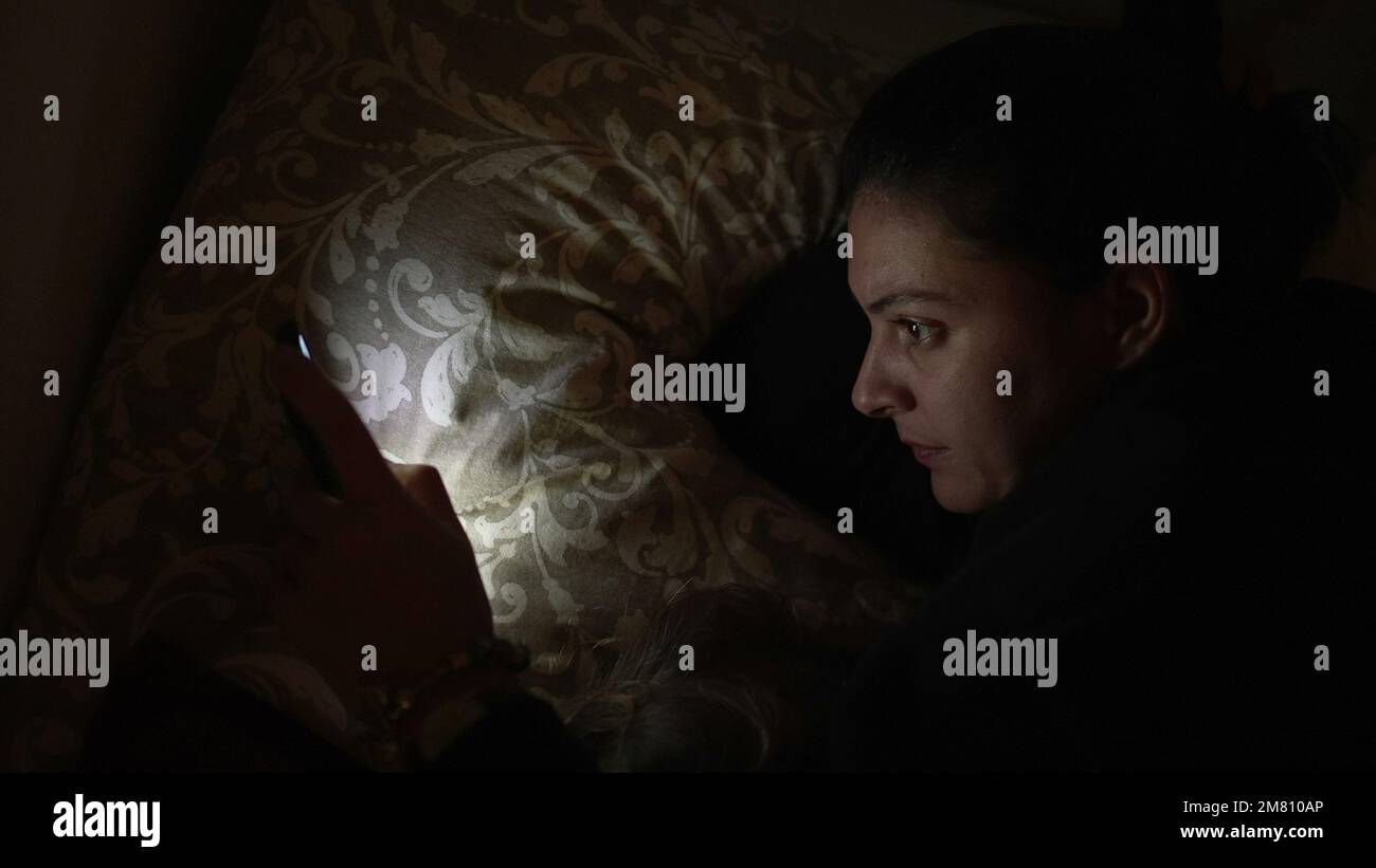 Woman staring at cellphone screen at night in bed. Person looks at ...