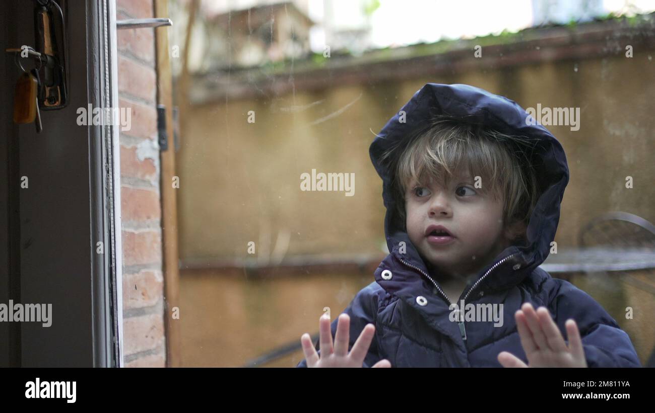 Toddler child leaning on window looking through glass. Baby two year ...