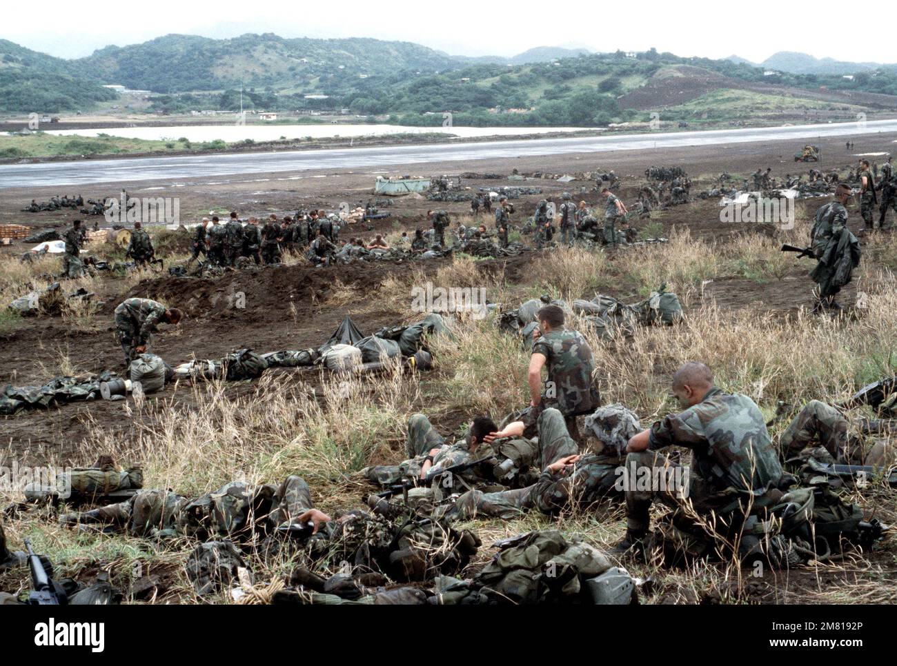 Members of the 82nd Airborne Division rest beside the runway during Operation URGENT FURY ...