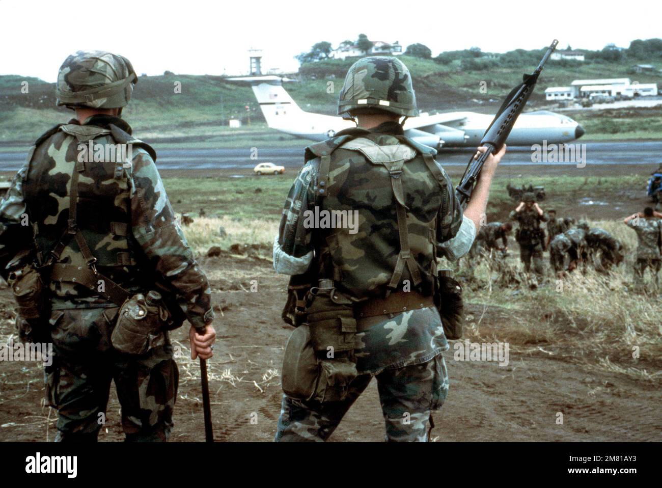 US military personnel, armed with M16A1 rifles, observe a C-141 ...