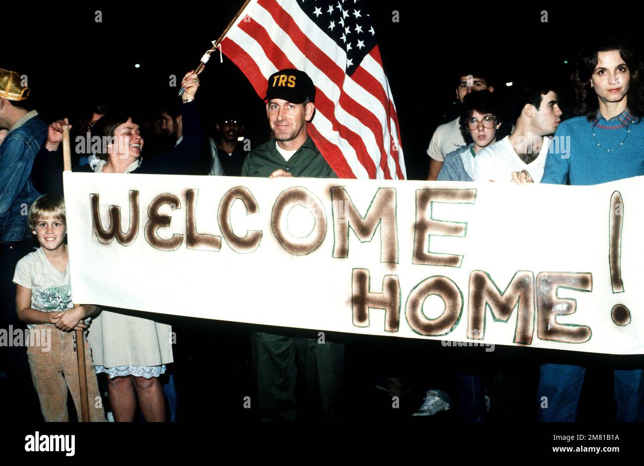 Friends and family members hold up a "Welcome Home" sign for the ...