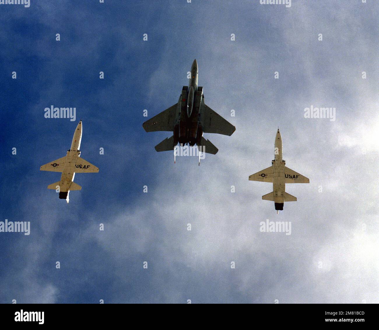 An air-to-air underside view of an F-15 Eagle aircraft leading two T-38 Talon aircraft in a ...