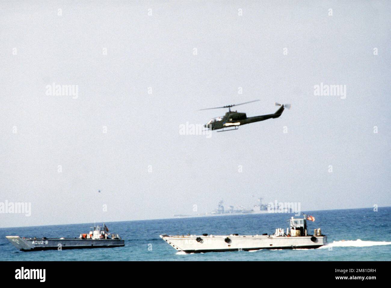 A Marine AH-1J Sea Cobra helicopter flies over two utility landing ...