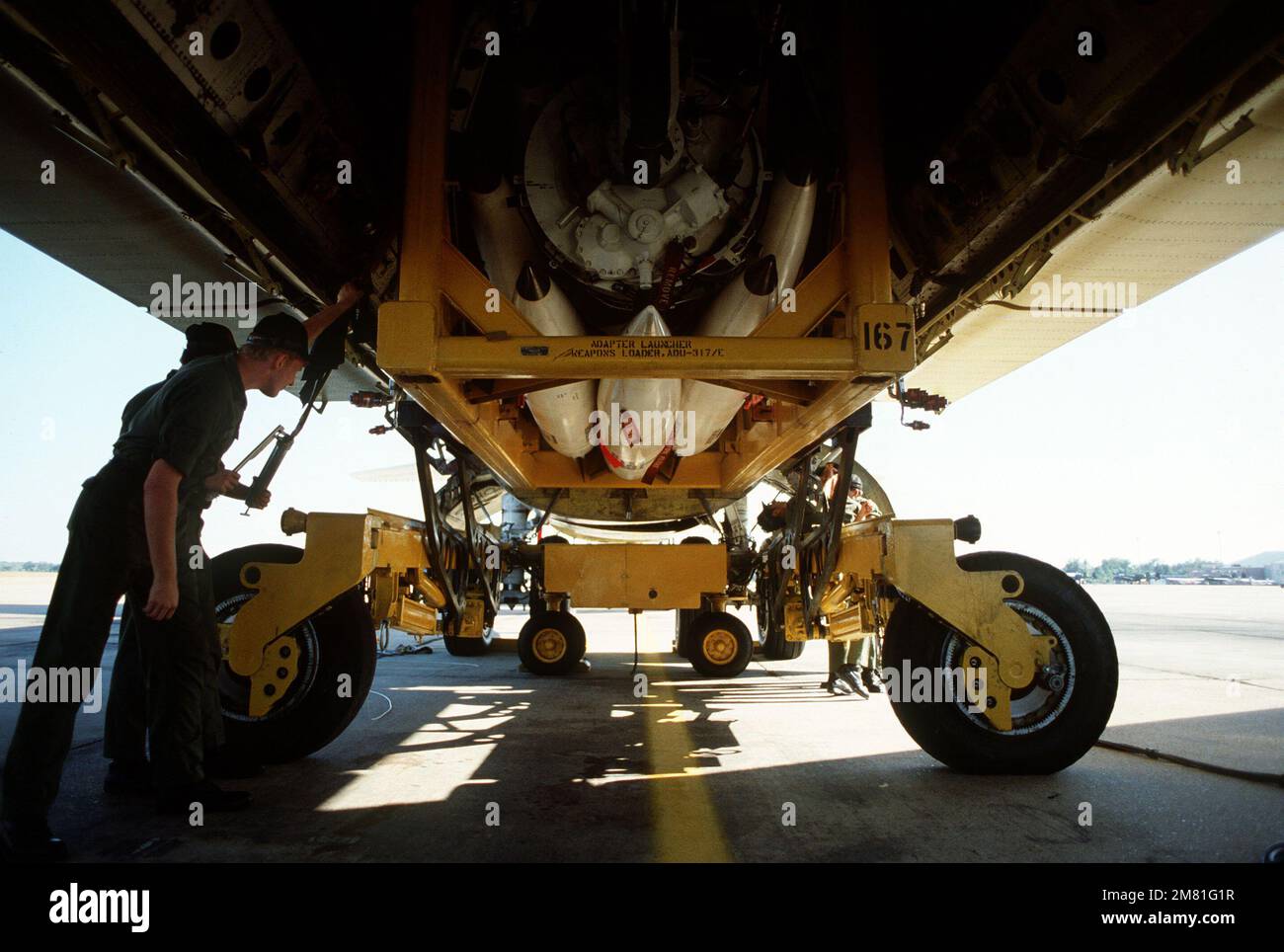 Munitions personnel use a weapons loader to load missiles into the bomb ...