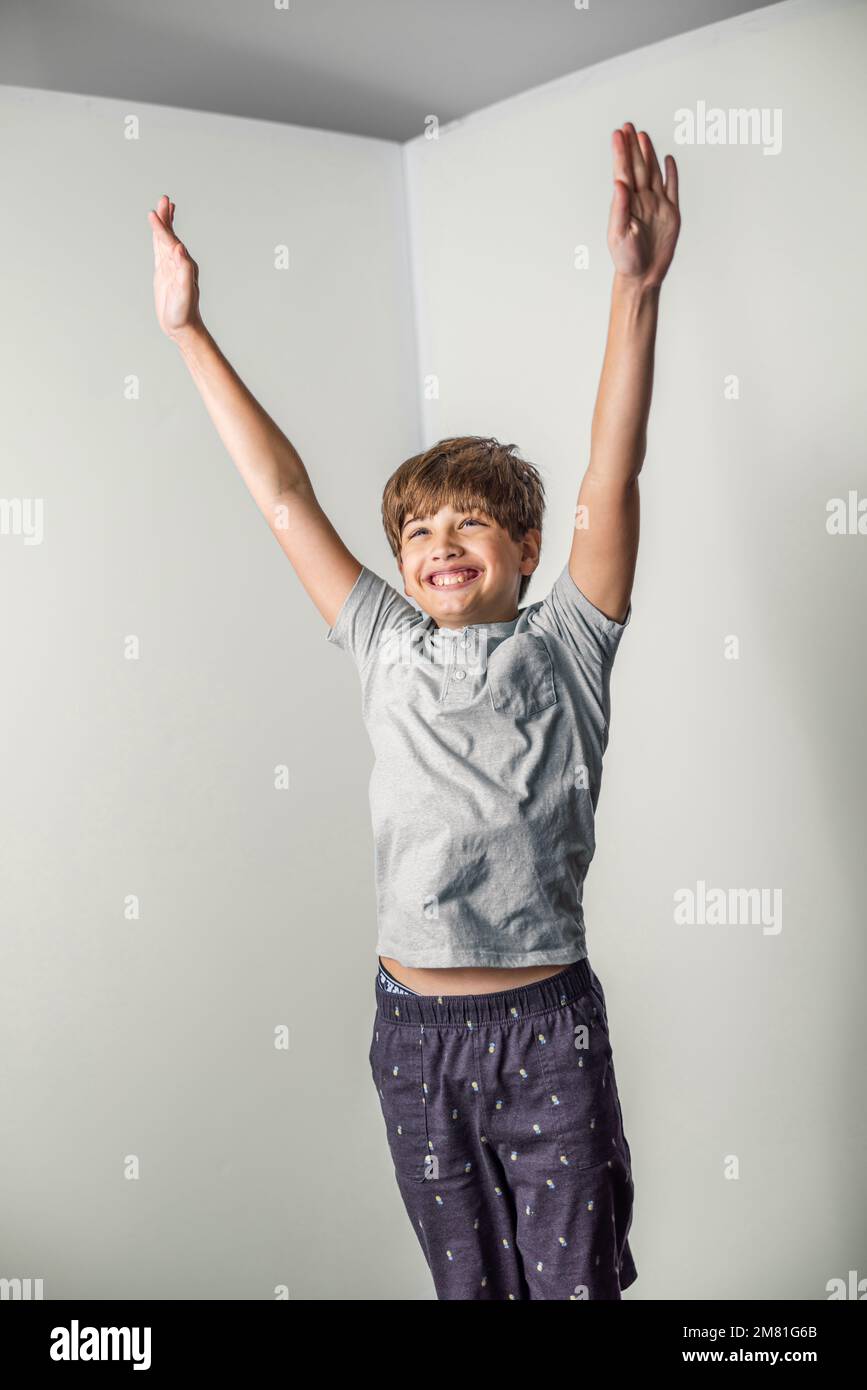A tween boy jumping up in the air in excitement against a white corner ...