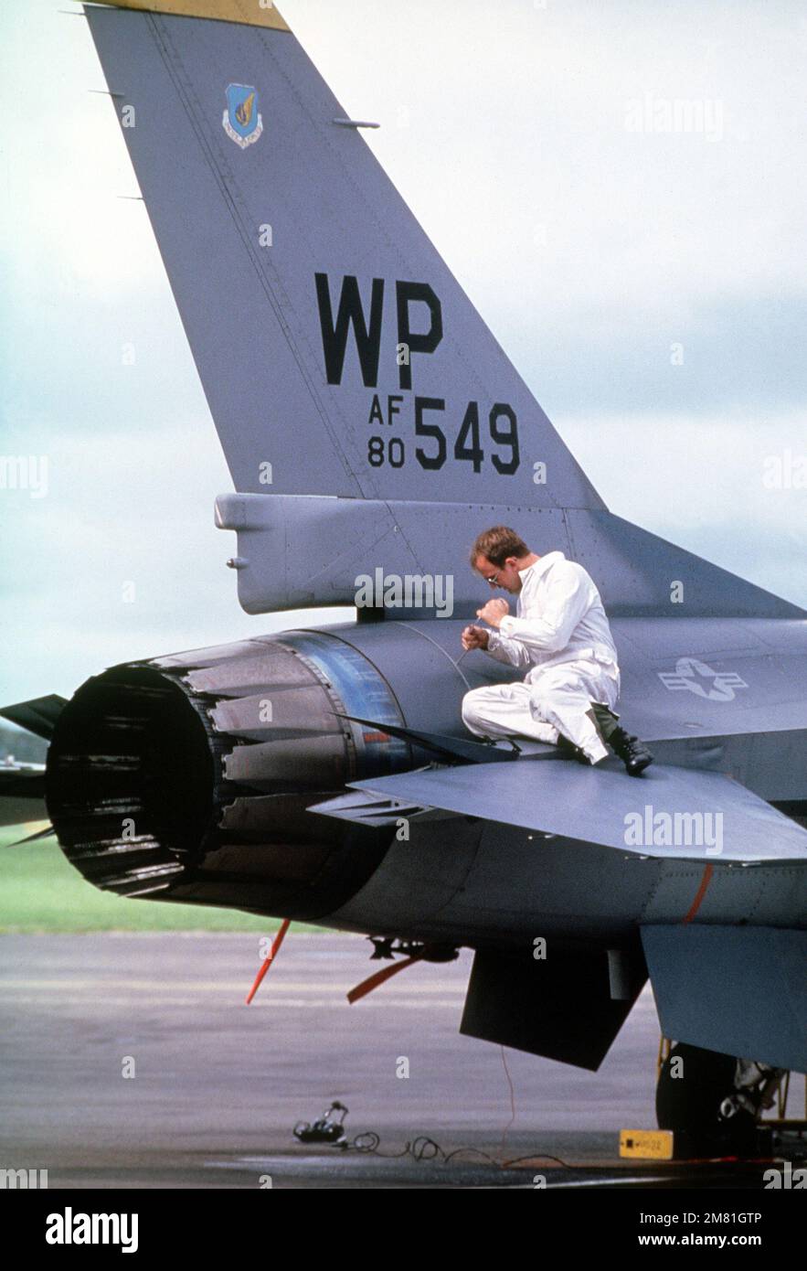 USAF maintenance technician, wearing white overalls tightens a panel on ...