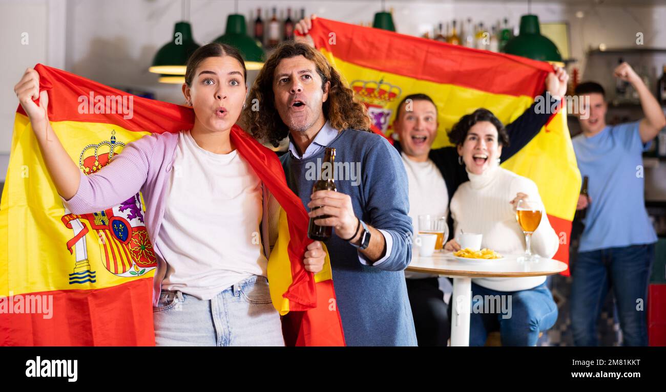 Company of excited young adult sports fans waving flag of Spain and ...