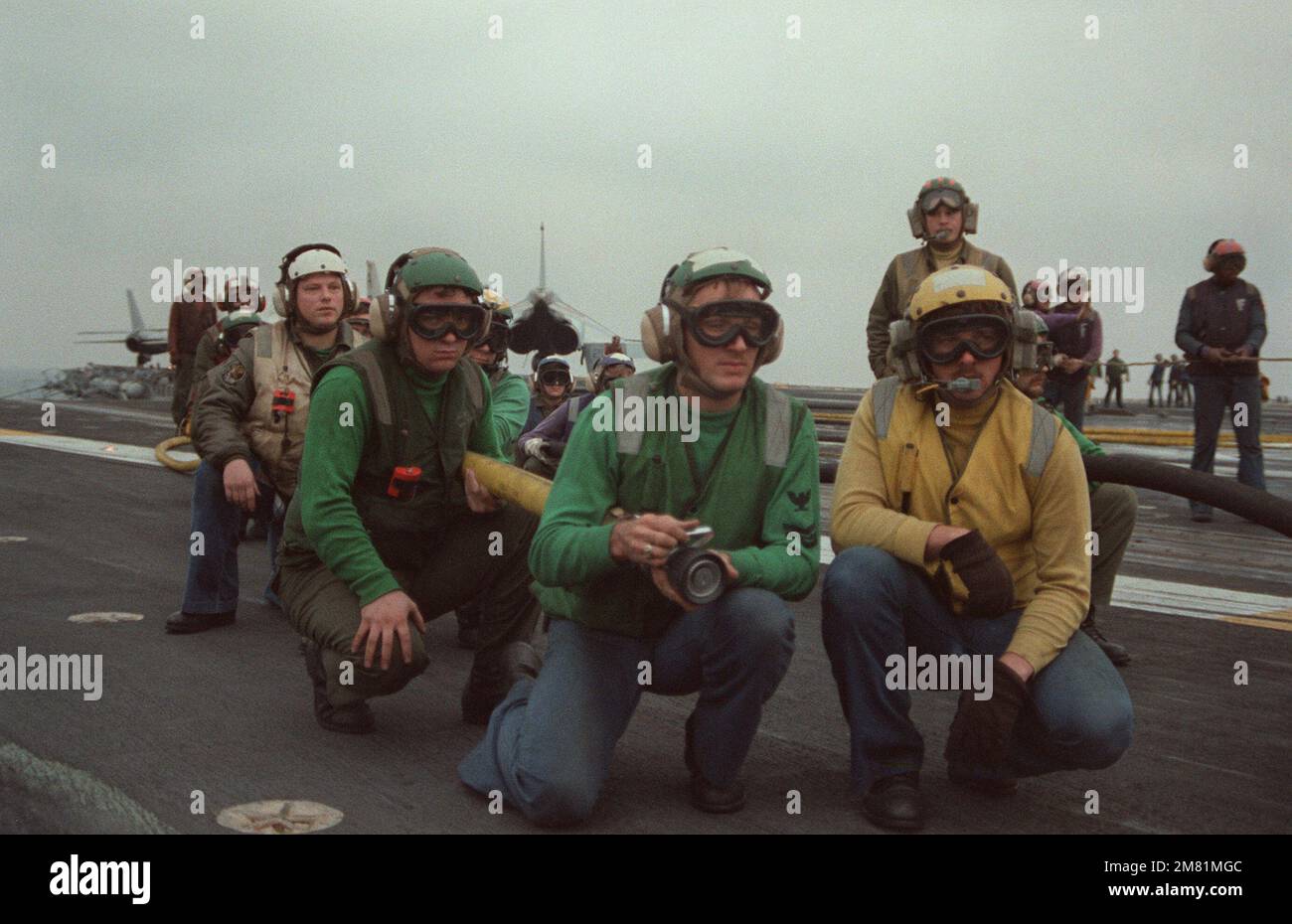 A fire fighting party stands by as crewman use a crane to pull an F-4 ...