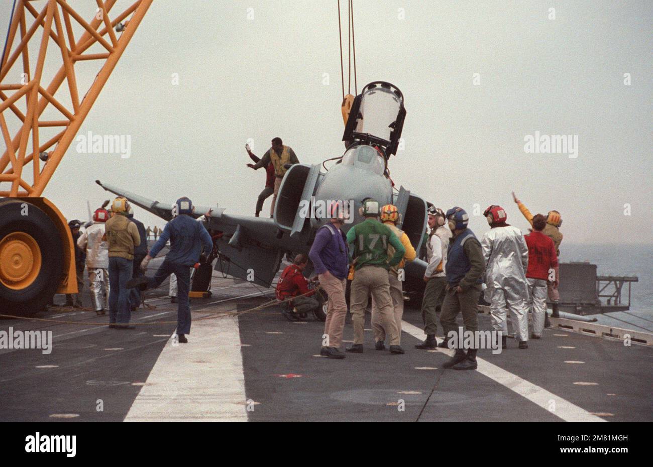 Crewman use a crane to pull an F-4 Phantom aircraft away from the edge ...
