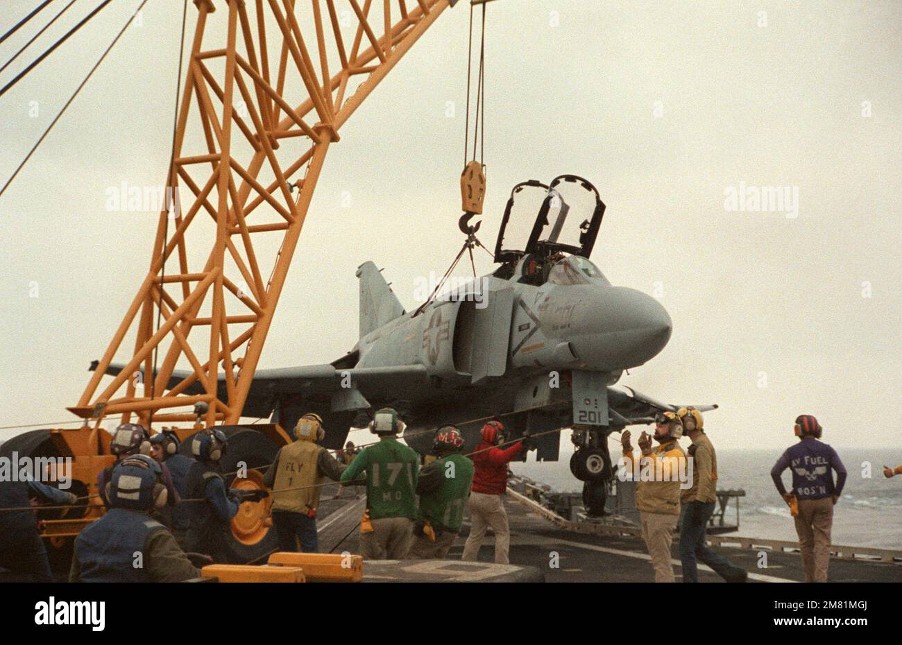 Crewman use a crane to pull an F-4 Phantom aircraft away from the edge ...