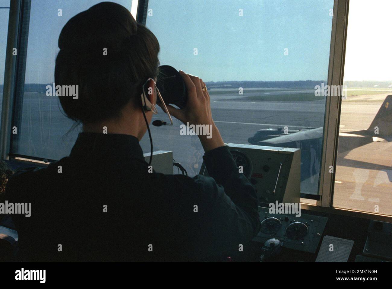 An air traffic controller checks the flight line with binoculars from ...