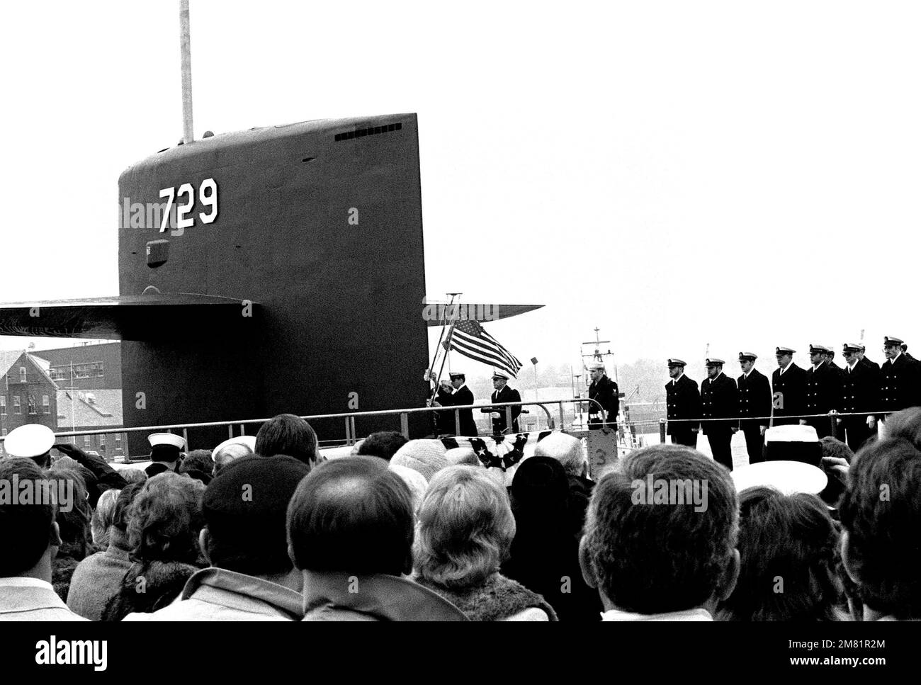 Crew members stand at attention as the US flag is raised aboard ship ...