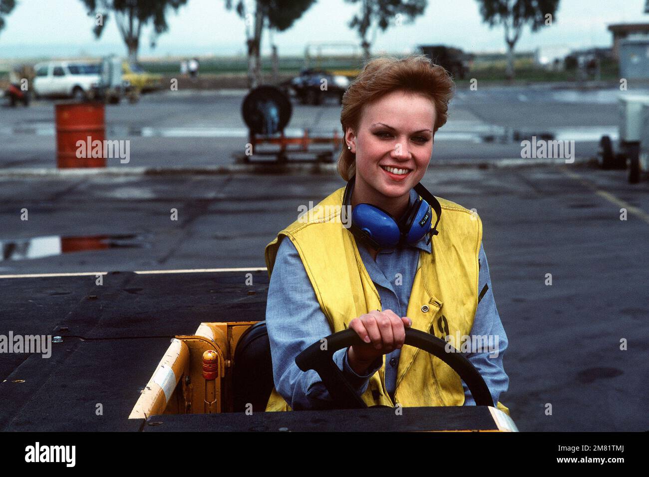 A female plane director drives a tow tractor on the flight line. Base ...