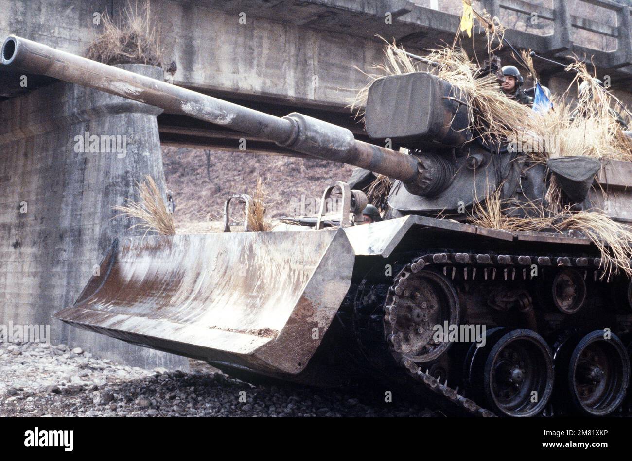 An M60 main battle tank, equipped with a bulldozer blade, sets up a ...