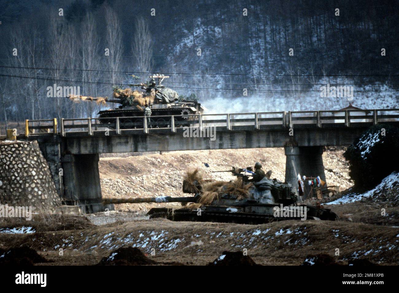 An M60 main battle tank crosses a bridge above another M60 dug into a ...