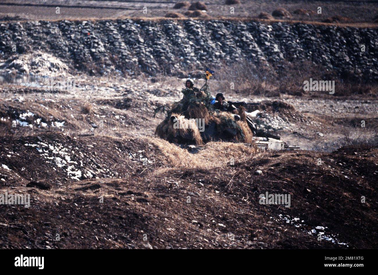 A camouflaged M60 main battle tank (Blue Team) is in a stream bed ...