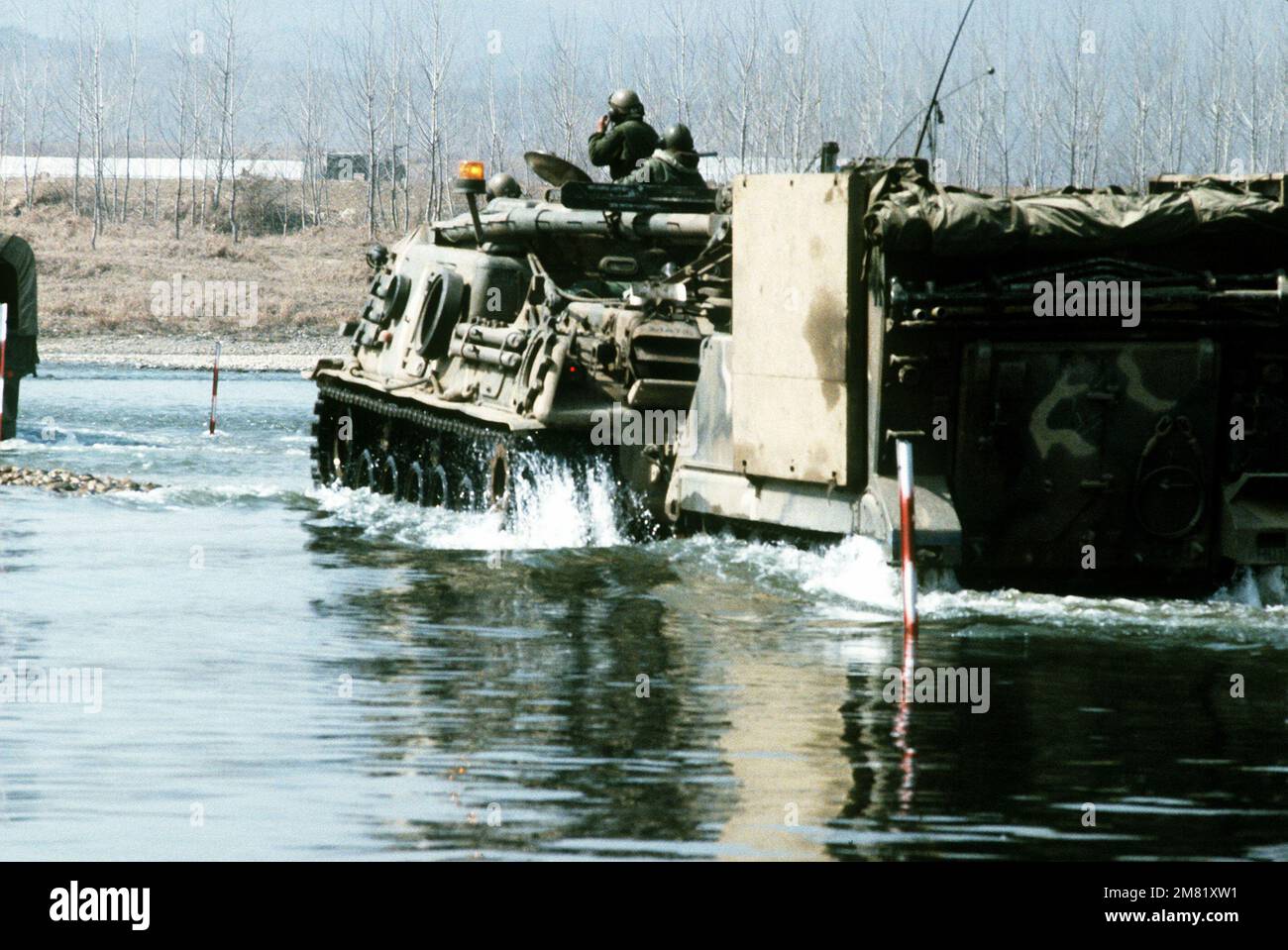 An armored M-88 armored recovery vehicle tows an M-113 armored ...