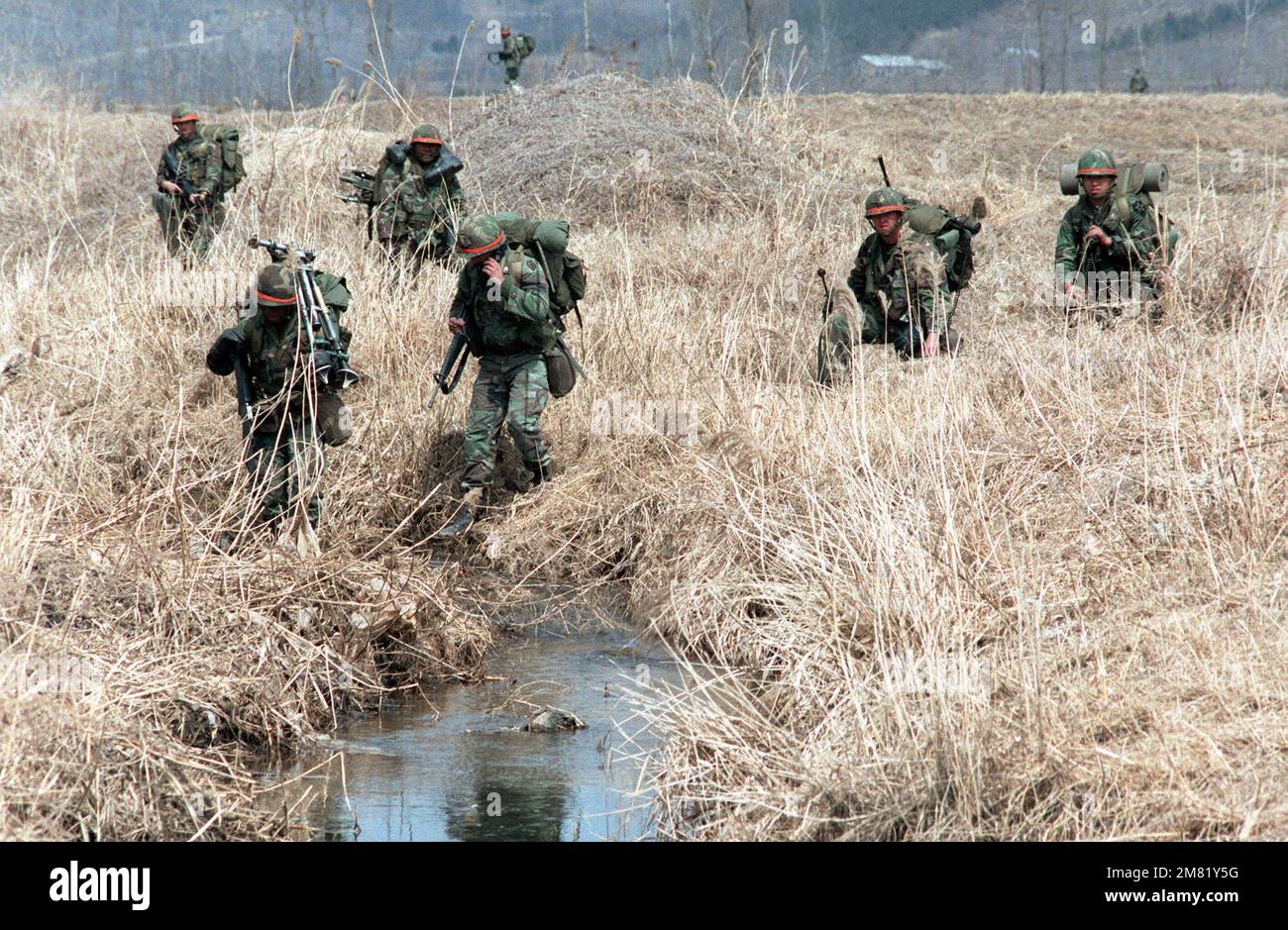 Soldiers carrying full backpacks of equipment move across a field ...