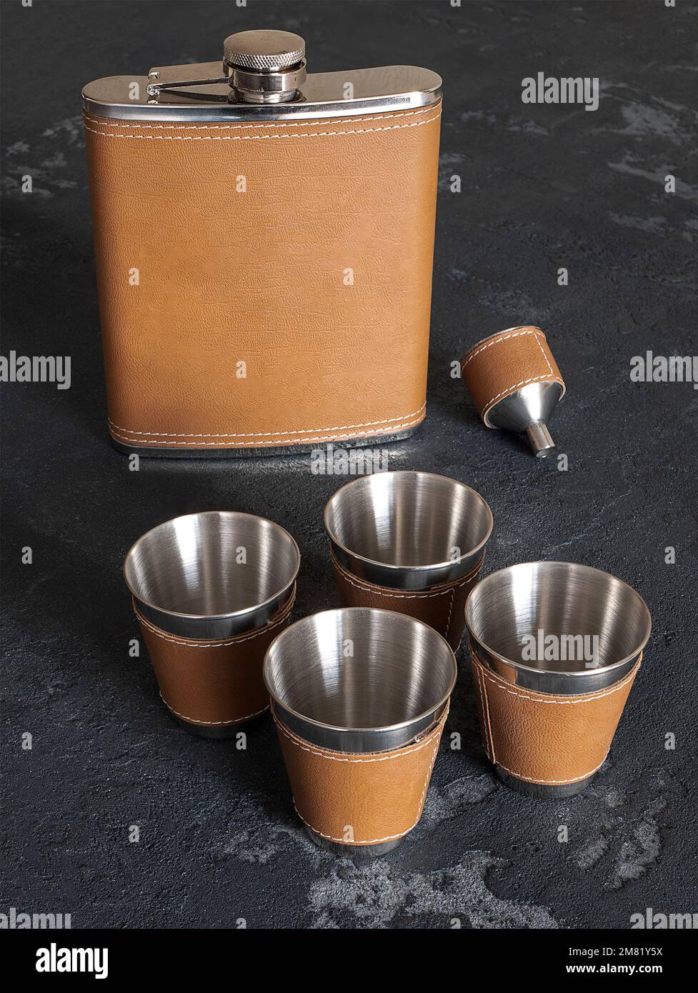 Hip flask made of stainless steel and brown leather with cups on a dark ...