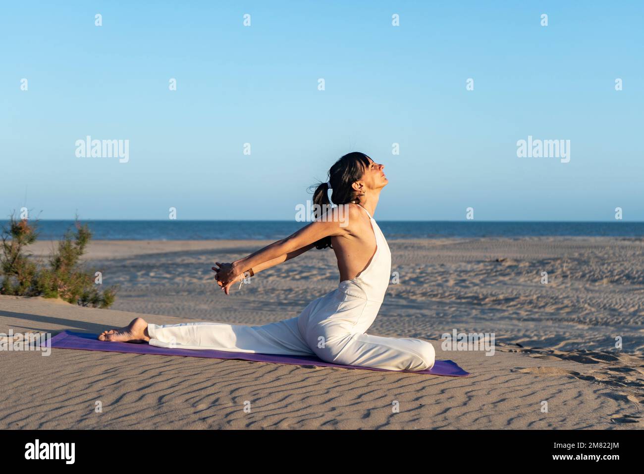 Side view of a woman practising yoga on a mat on the beach Stock Photo ...