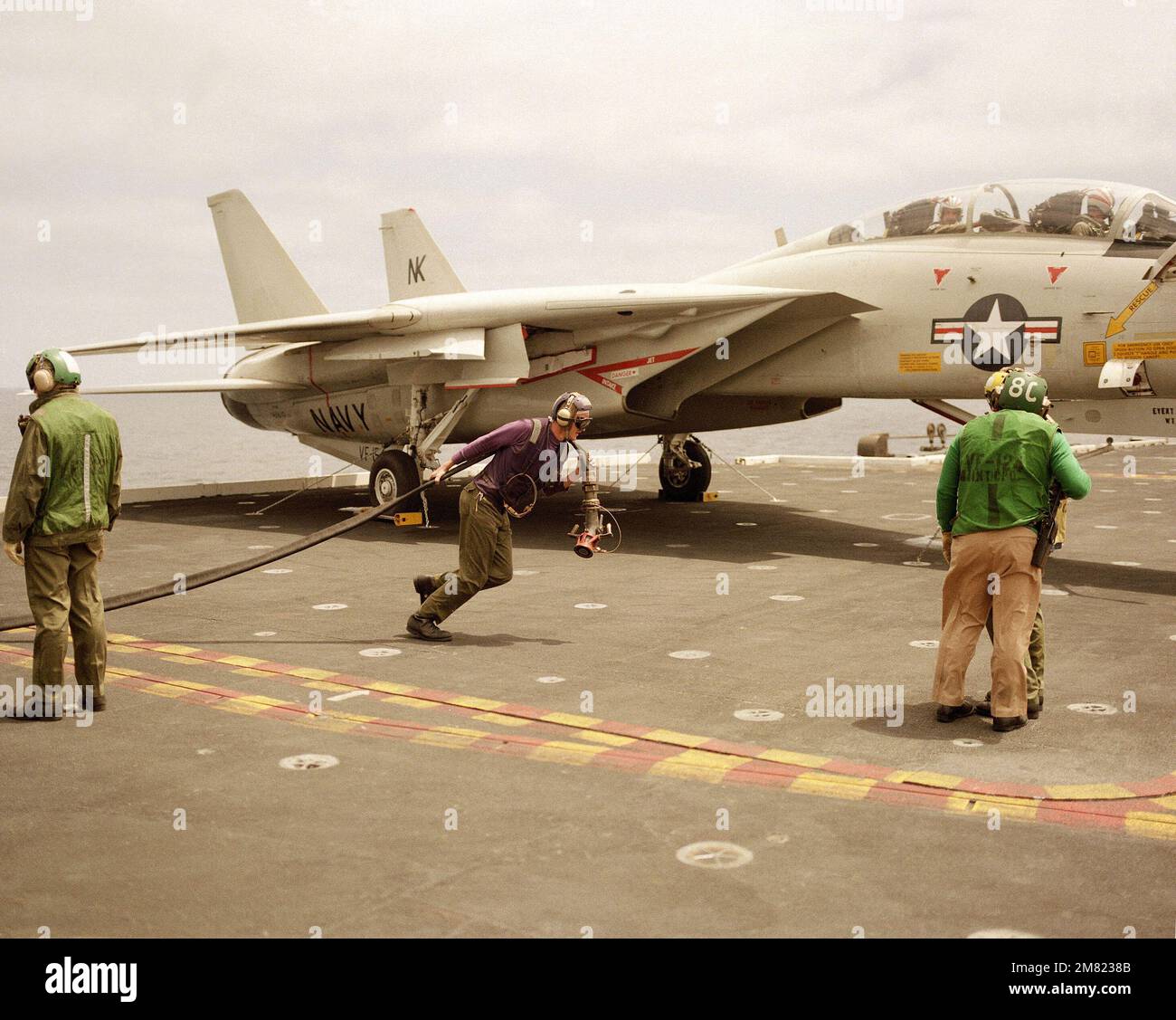 An aviation boatswain's mate (fuels) hauls a fuel hose to an F-14 ...