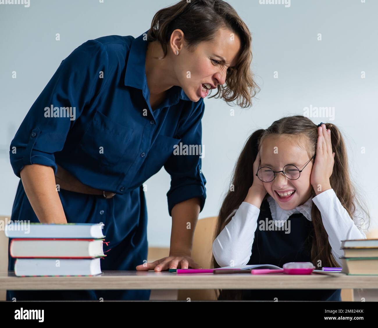 A female teacher yells at a student. Little girl covers her ears with ...