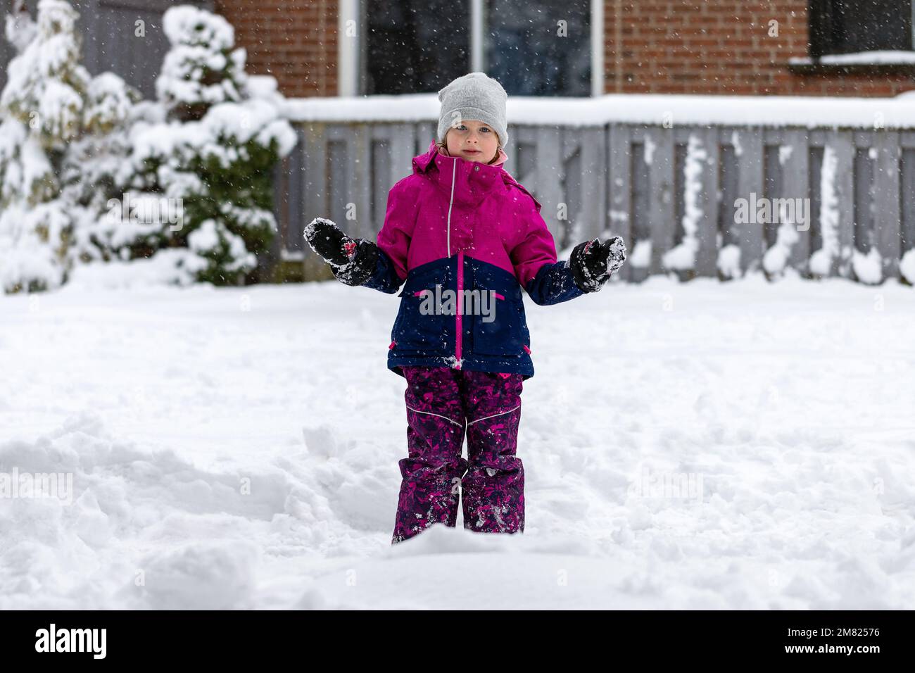Little child standing outside near house in winter on snow day ...