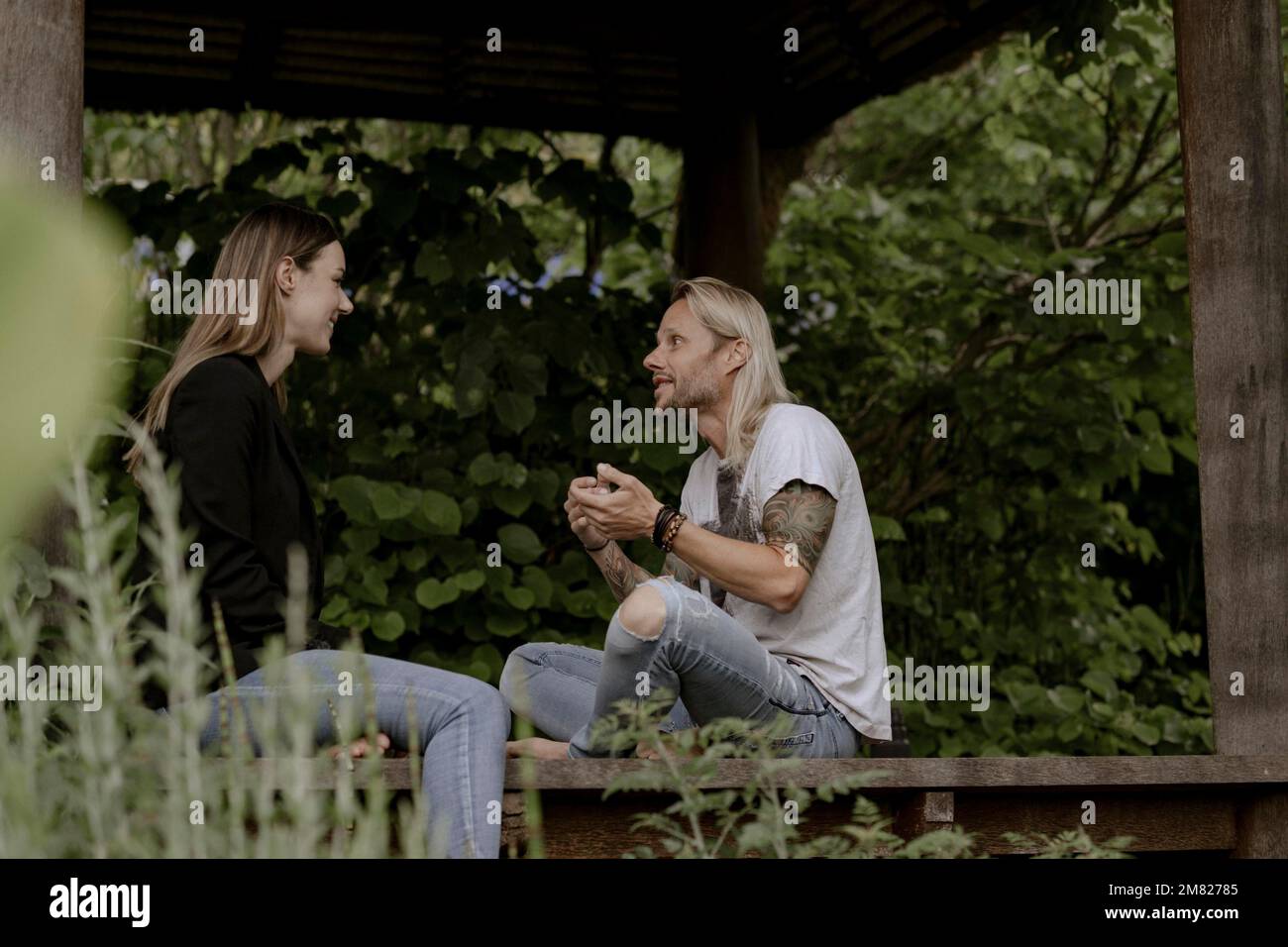 Tattooed man in conversation with woman in greenery Stock Photo - Alamy