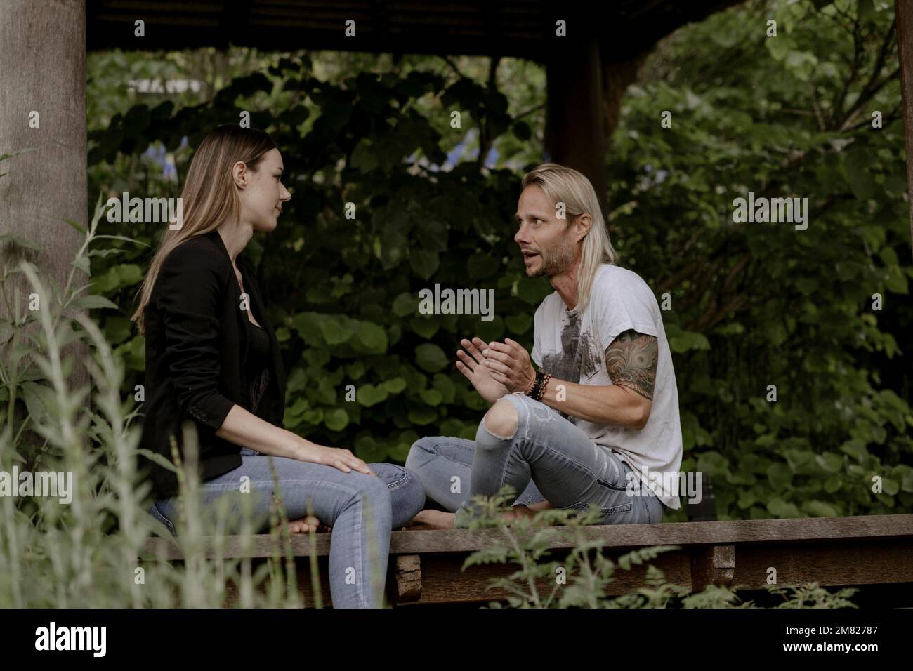 Tattooed man in conversation with woman in greenery Stock Photo - Alamy