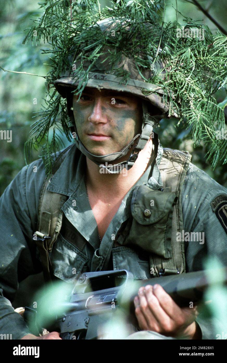 A soldier wearing camouflage, armed with an M16A1 rifle, takes cover in ...