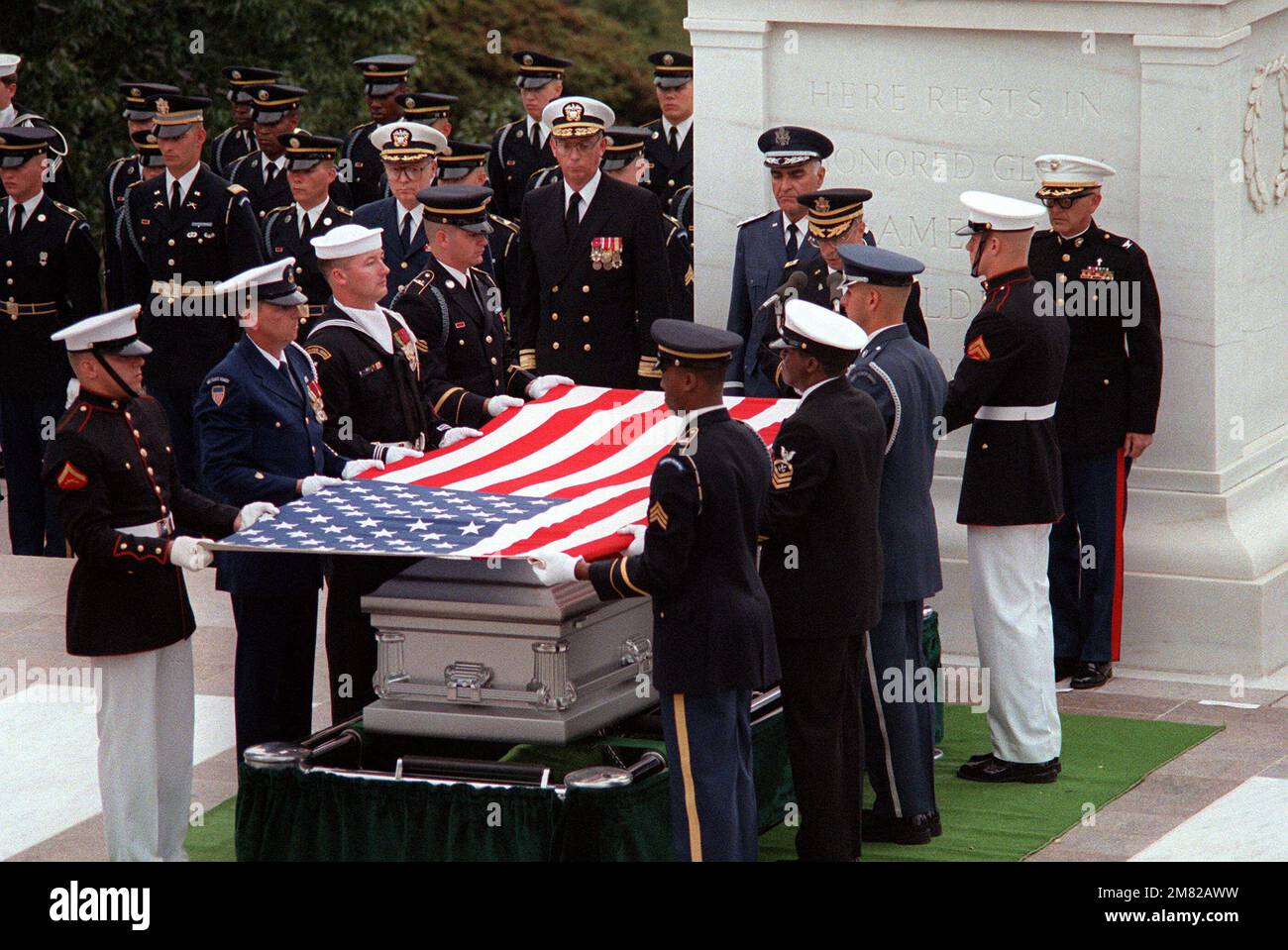 A joint services casket team holds the flag above the casket, as ...