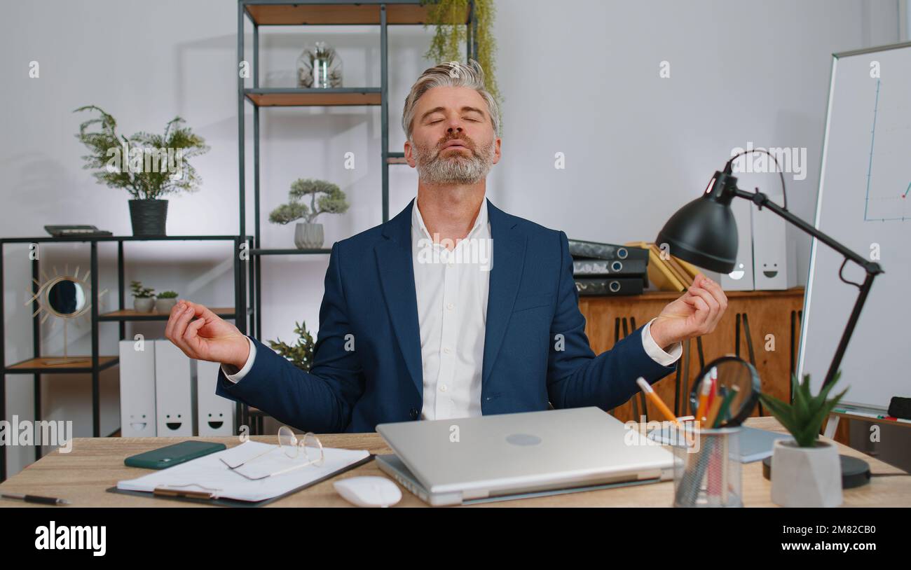 Mature businessman working on laptop computer, meditating, doing yoga ...