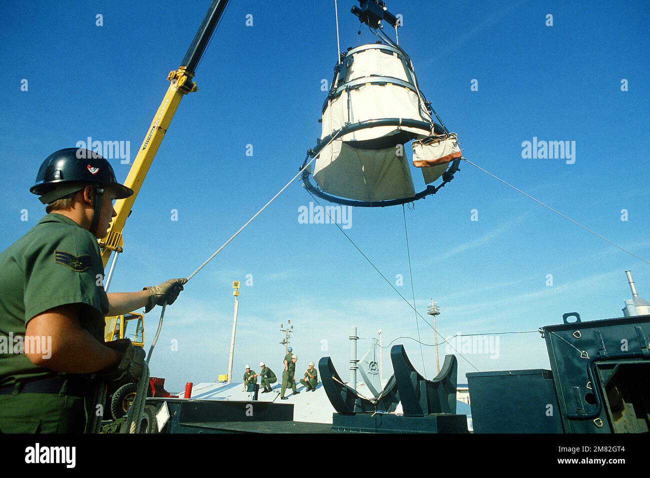 A crane lowers a reentry vehicle collar into a silo as members of the ...
