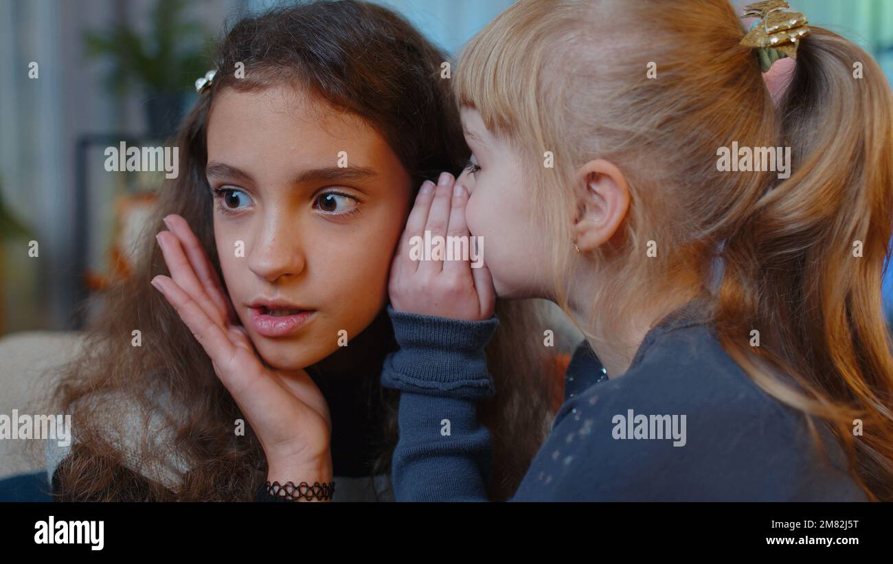 Teenage child whisper news rumors in ear to little sister kid girl ...