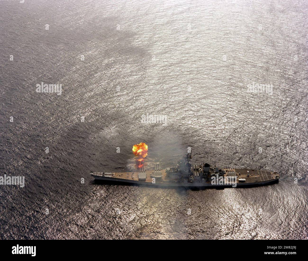 An elevated port beam view of the battleship USS IOWA (BB-61) as a round is fired from the No ...