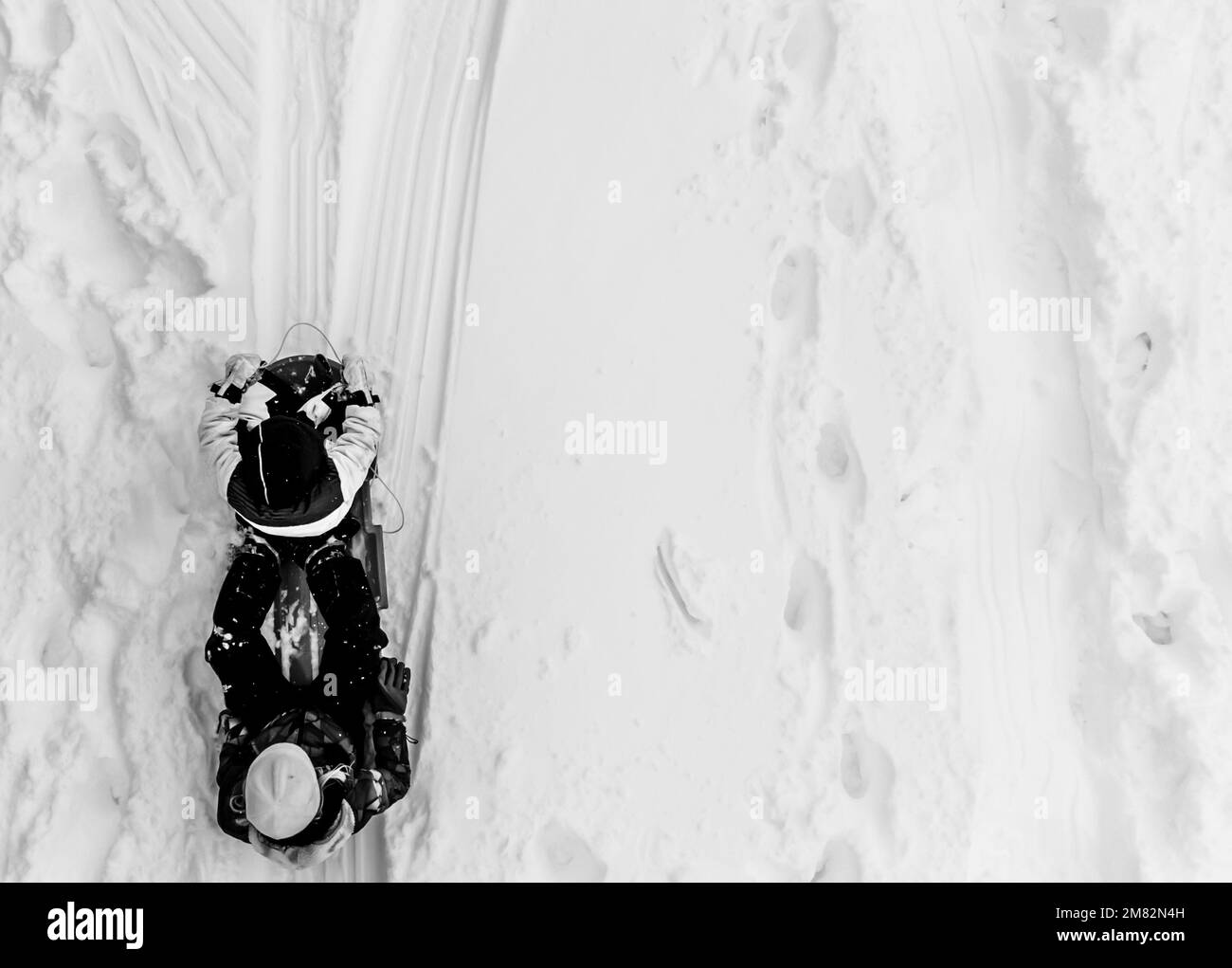 Aerial overhead done photo of two children in a sled going down a snow ...