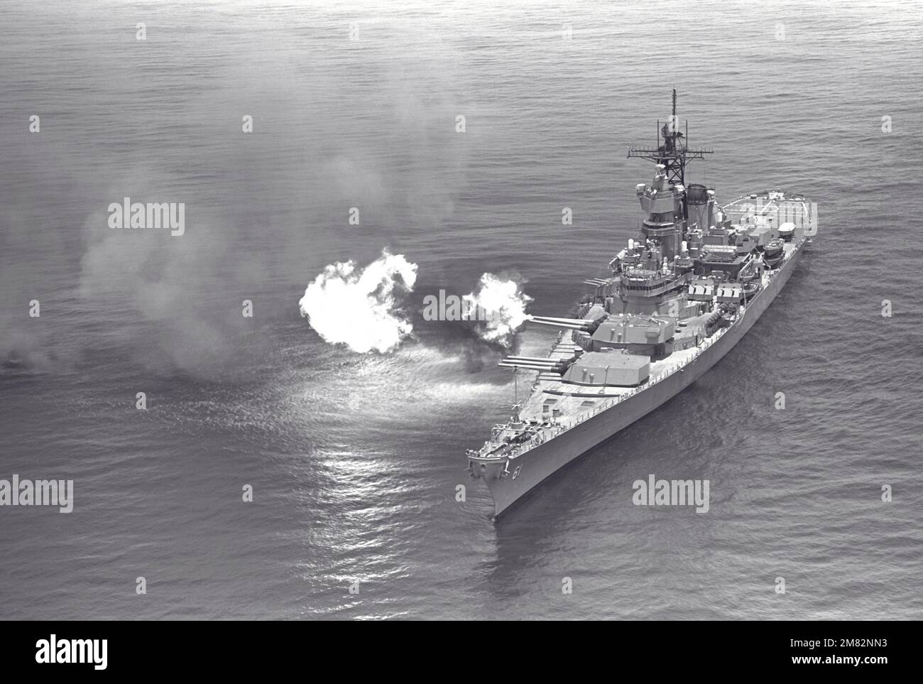 An aerial port bow view of the battleship USS IOWA (BB-61) firing a ...